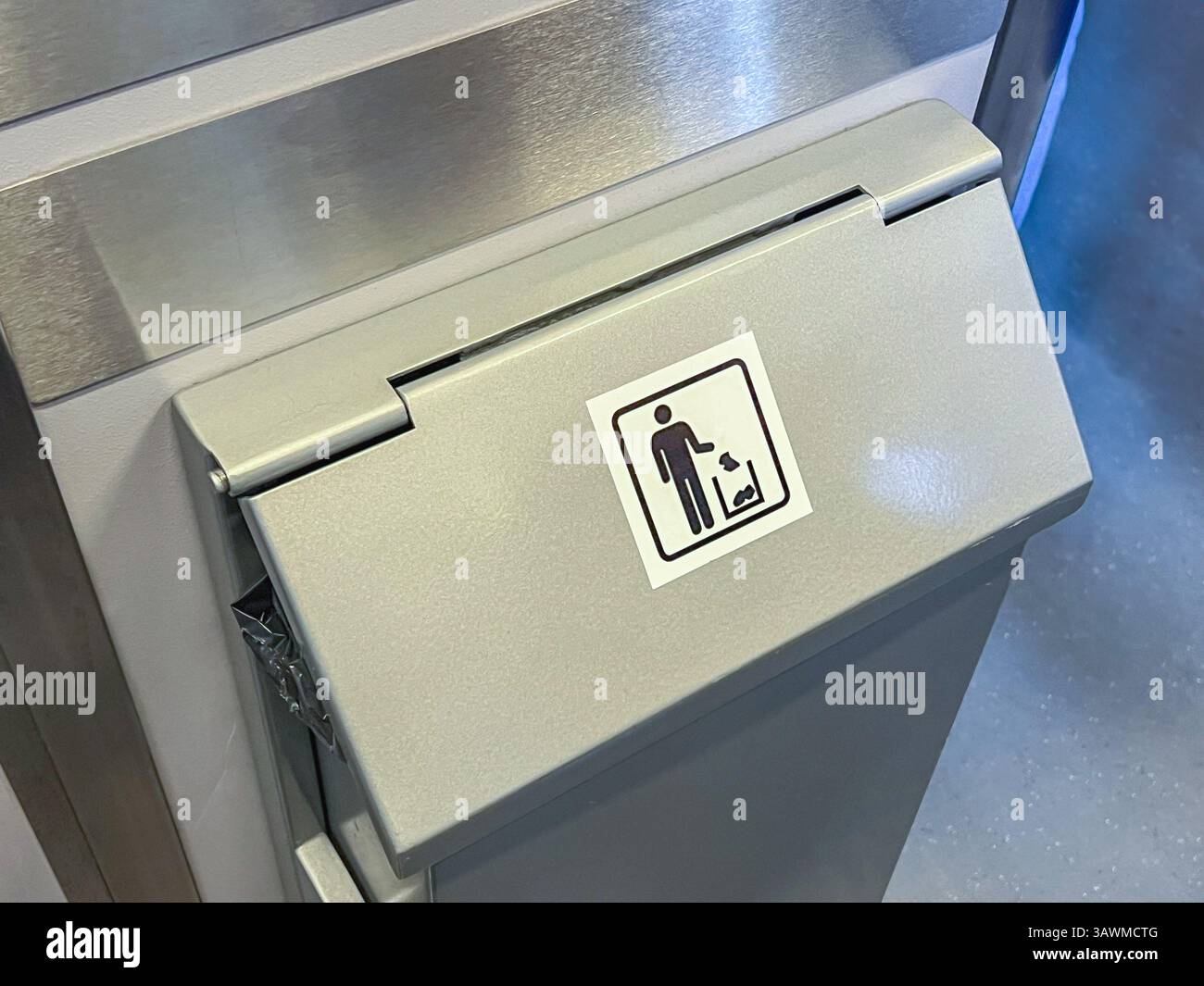 A close-up view of a metallic trash bin with a waste disposal sign ...