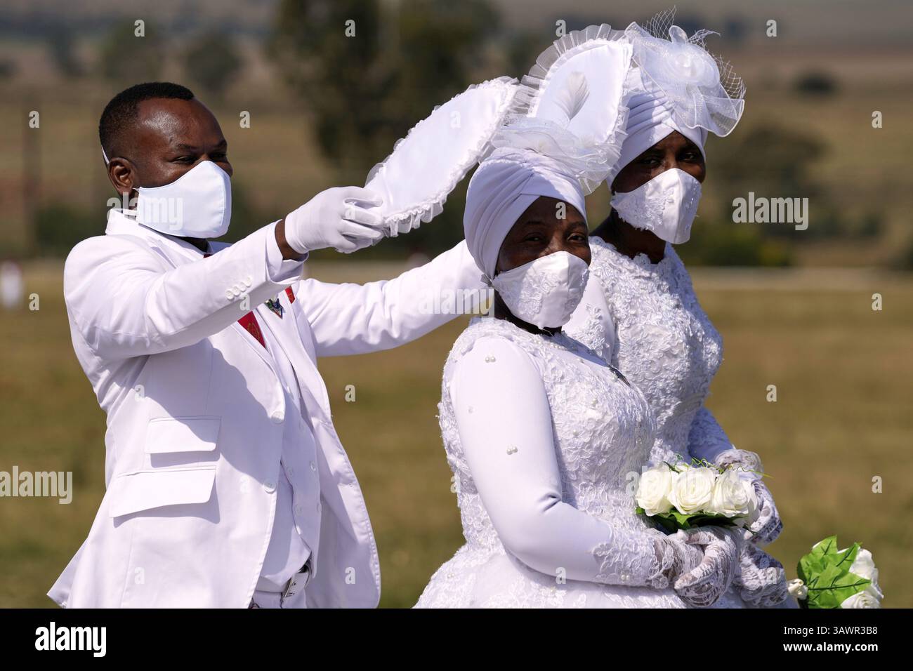 A groomsman shield his brides from the sun as they queue during a mass ...