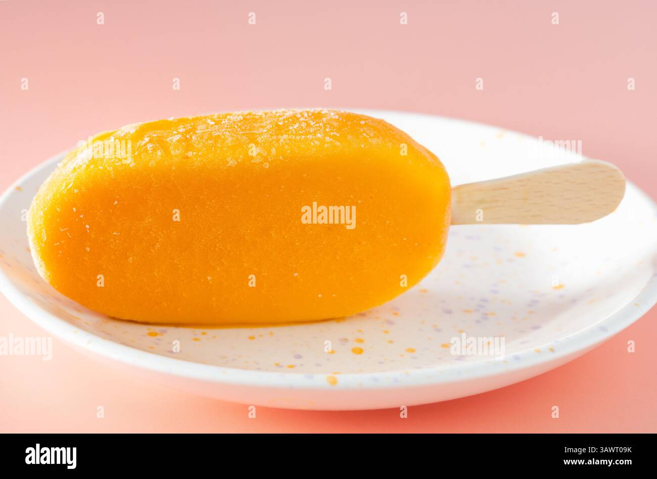 A close-up shows a bright orange popsicle starting to melt on a white ...