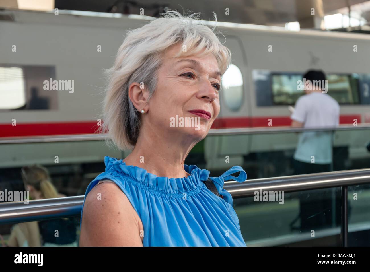 A middle-aged woman in a blue dress at a railway station, waiting for a ...