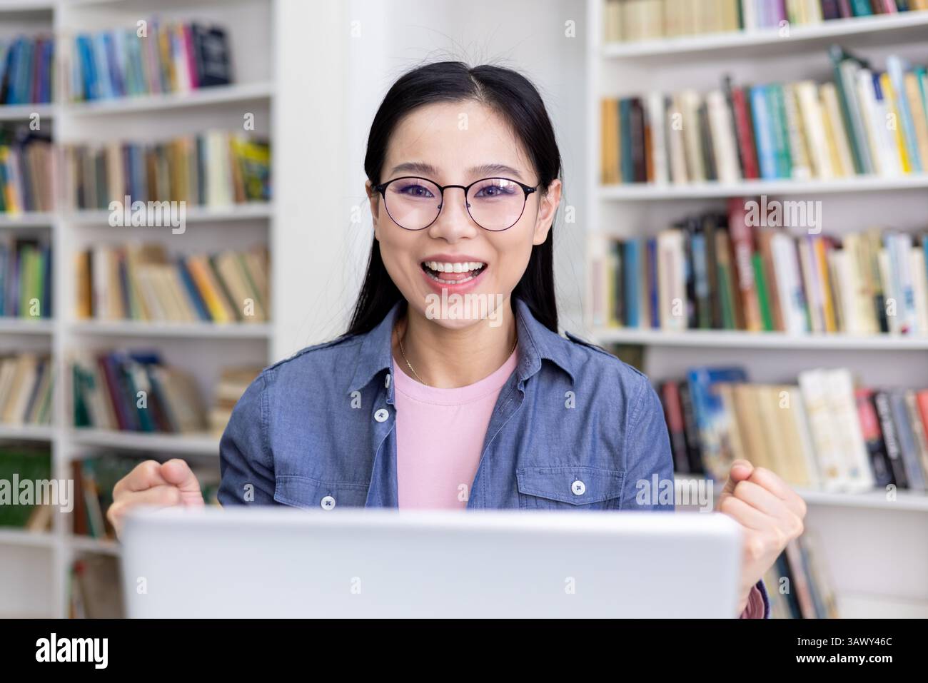 An excited asian woman wears glasses and looks at a laptop with an open ...