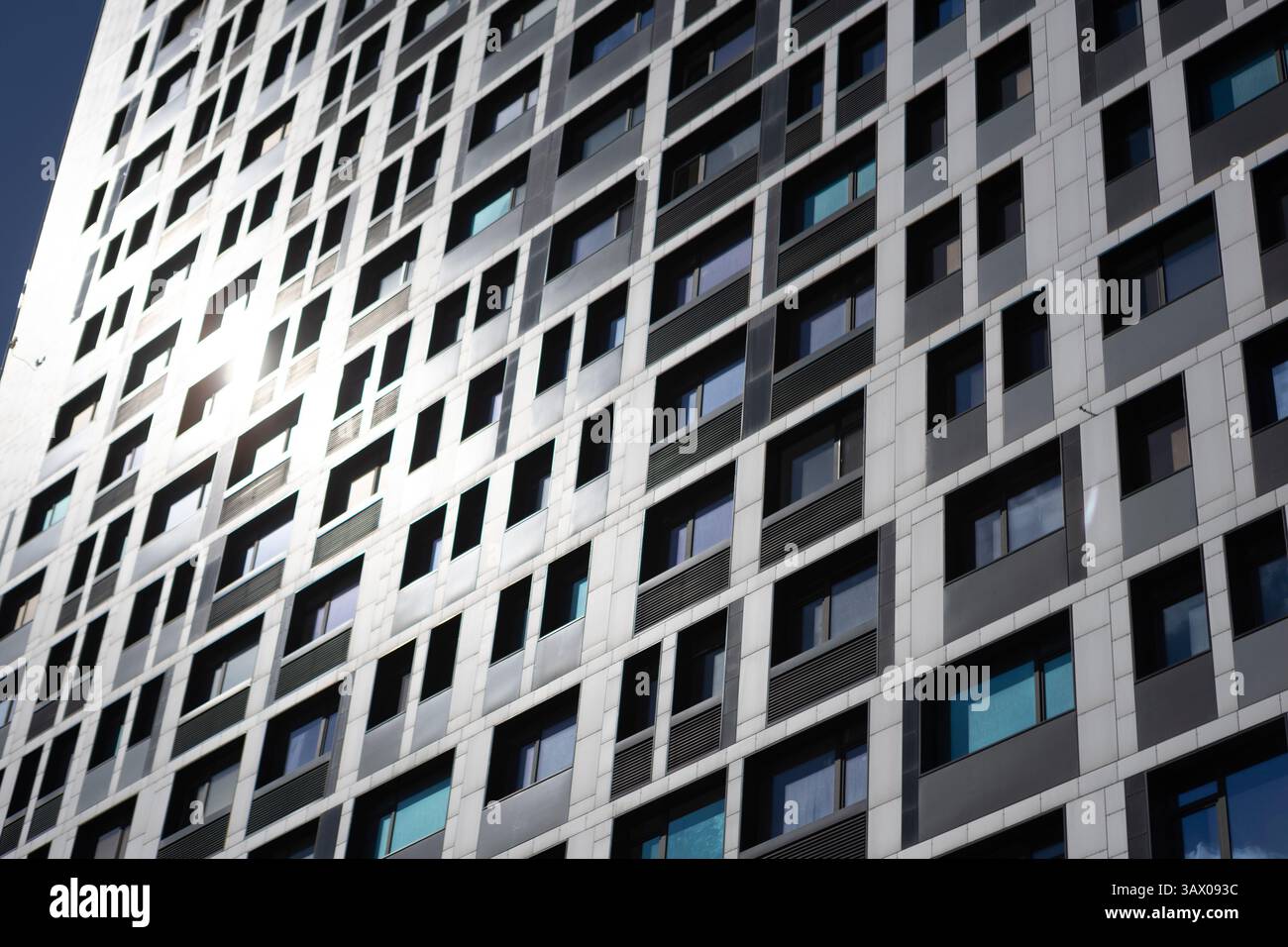 Facade of a tall residential building with sunlit windows reflecting ...