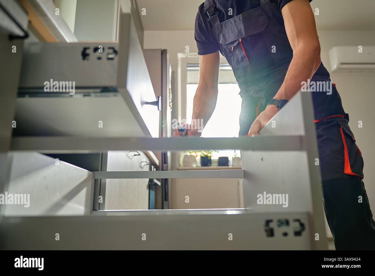 Man assembling kitchen drawer in modern cabinet using screwdriver ...