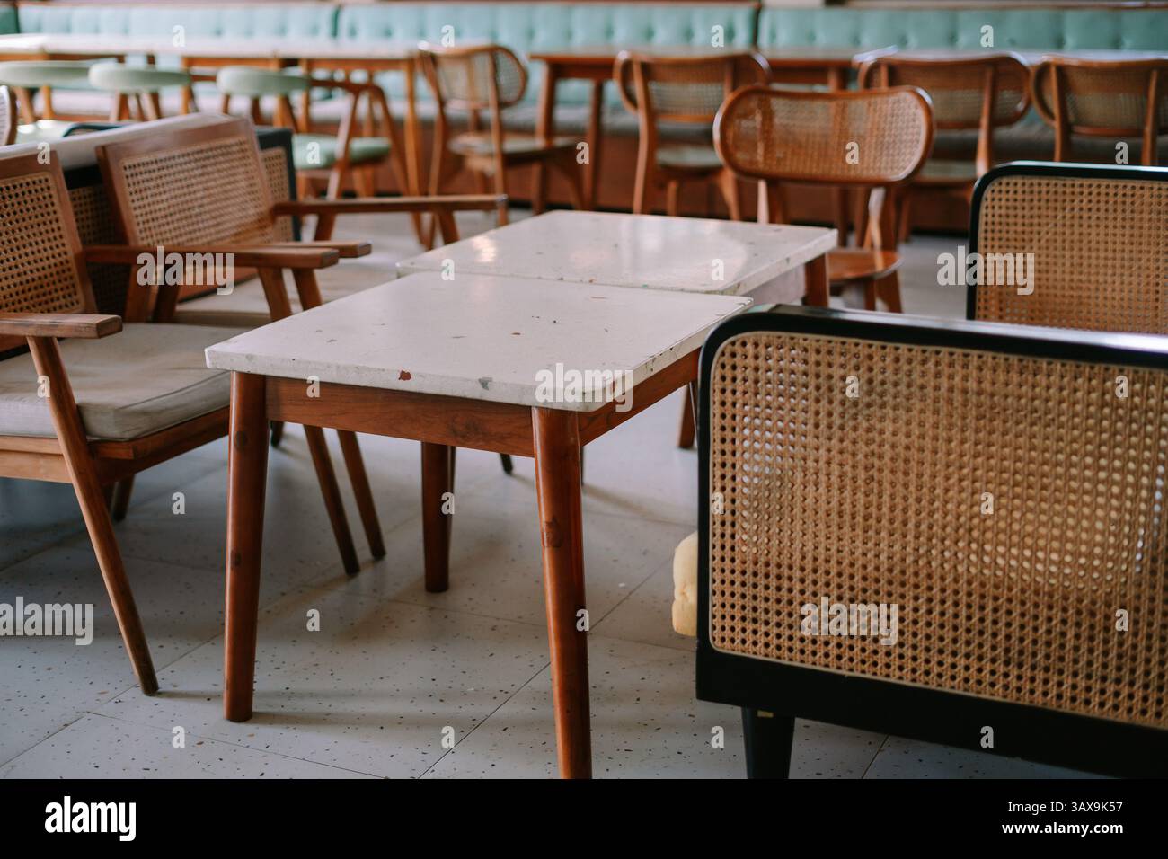 A stylish vintage cafe interior features rattan chairs and marble tables, creating a retro and ...