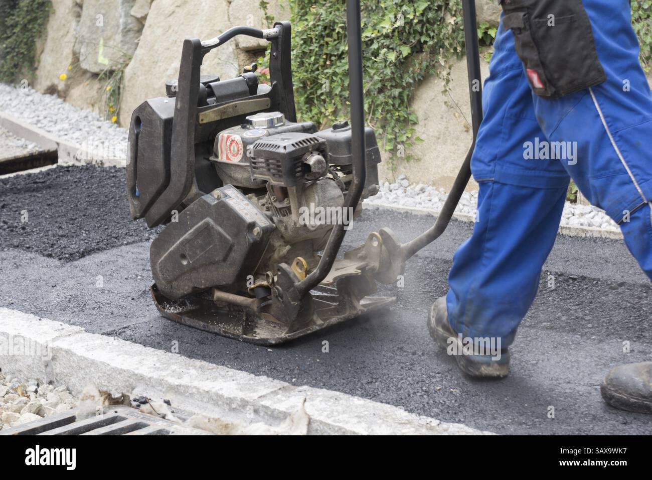 Construction worker with vibratory plate during pavement asphalting ...
