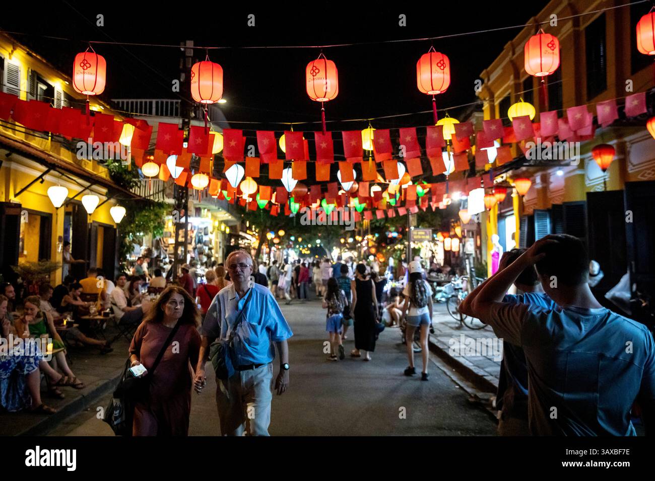 Tourism in Hoi An, Vietnam Tourists walk along a narrow street adorned ...