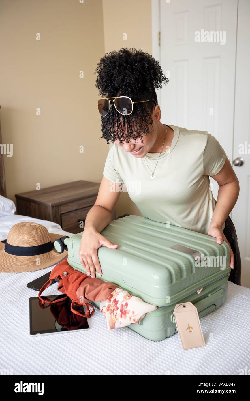 Woman laughs while trying to zip an overflowing suitcase shut Stock ...