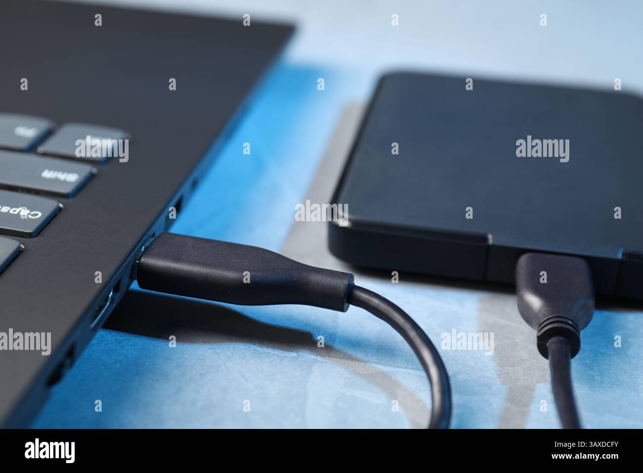 Hard disk drive with USB cable connected to laptop on blue textured ...