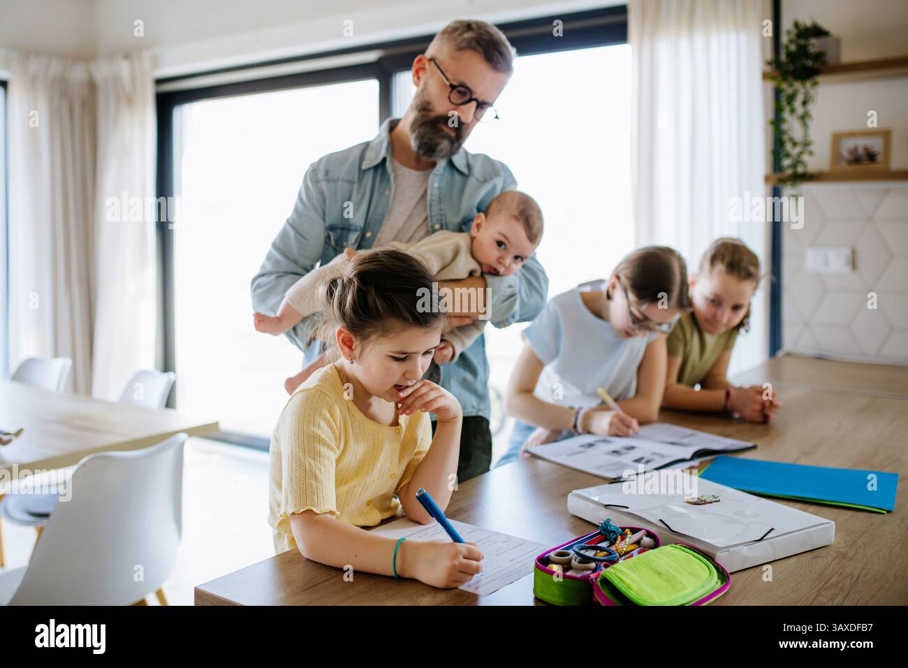 Father helping his daughters with homework while taking care of baby ...