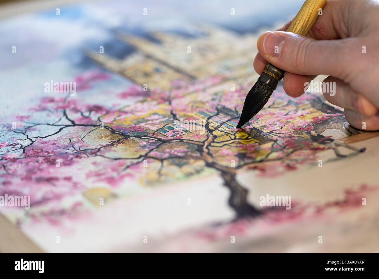 A man's hand holding a loaded brush and painting a cherry blossom tree ...