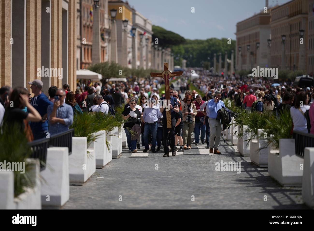 A man is followed by faithful as he holds a cross next to St. Peter's ...