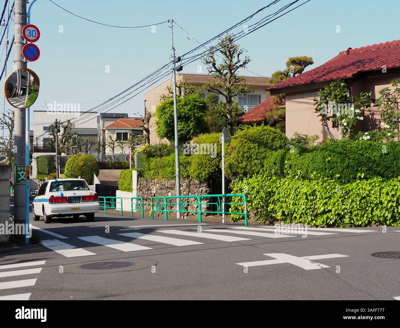 Suburban Tokyo street in late spring with greenery and white taxi ...