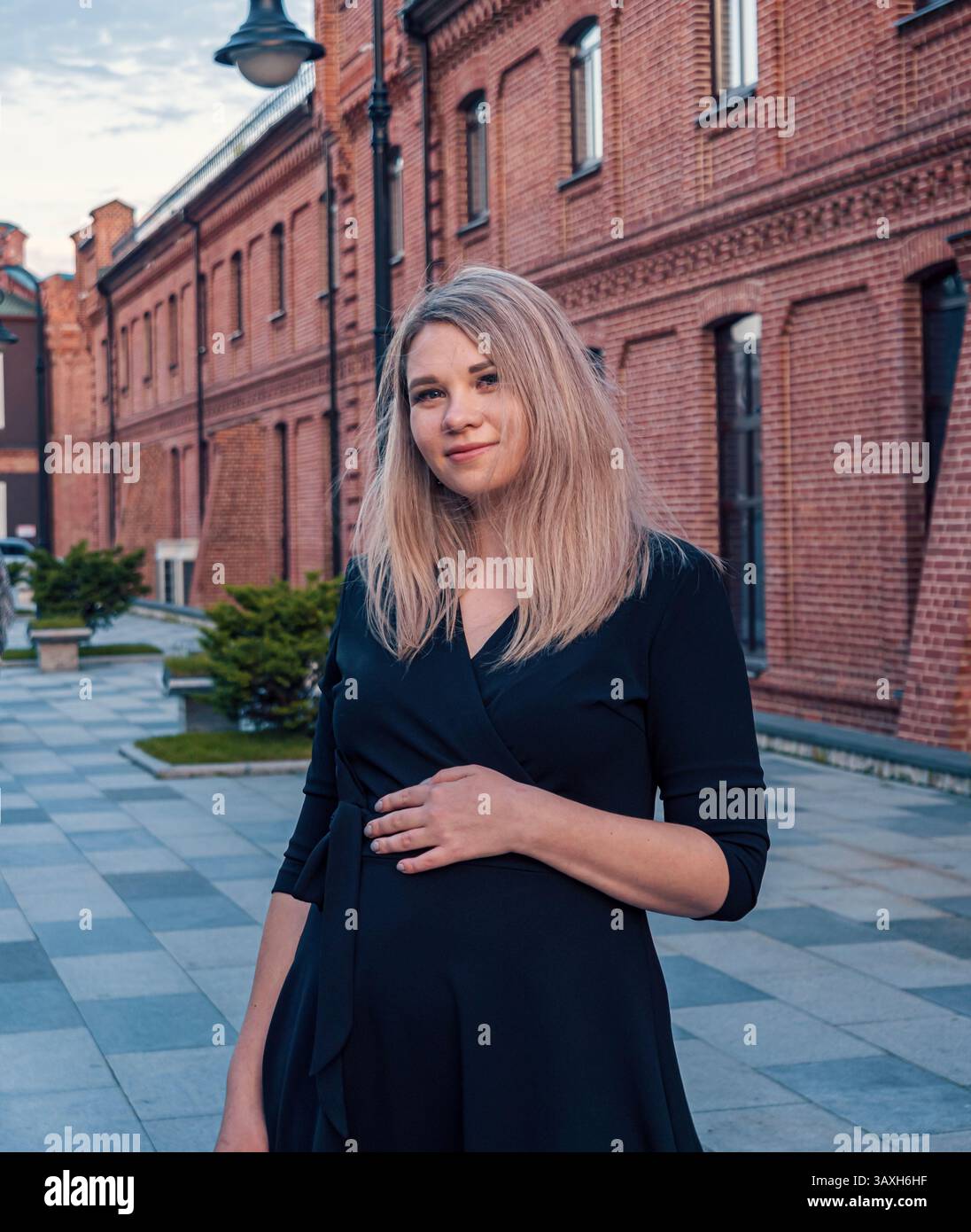 Pregnant woman in a black dress poses confidently outside historic red ...
