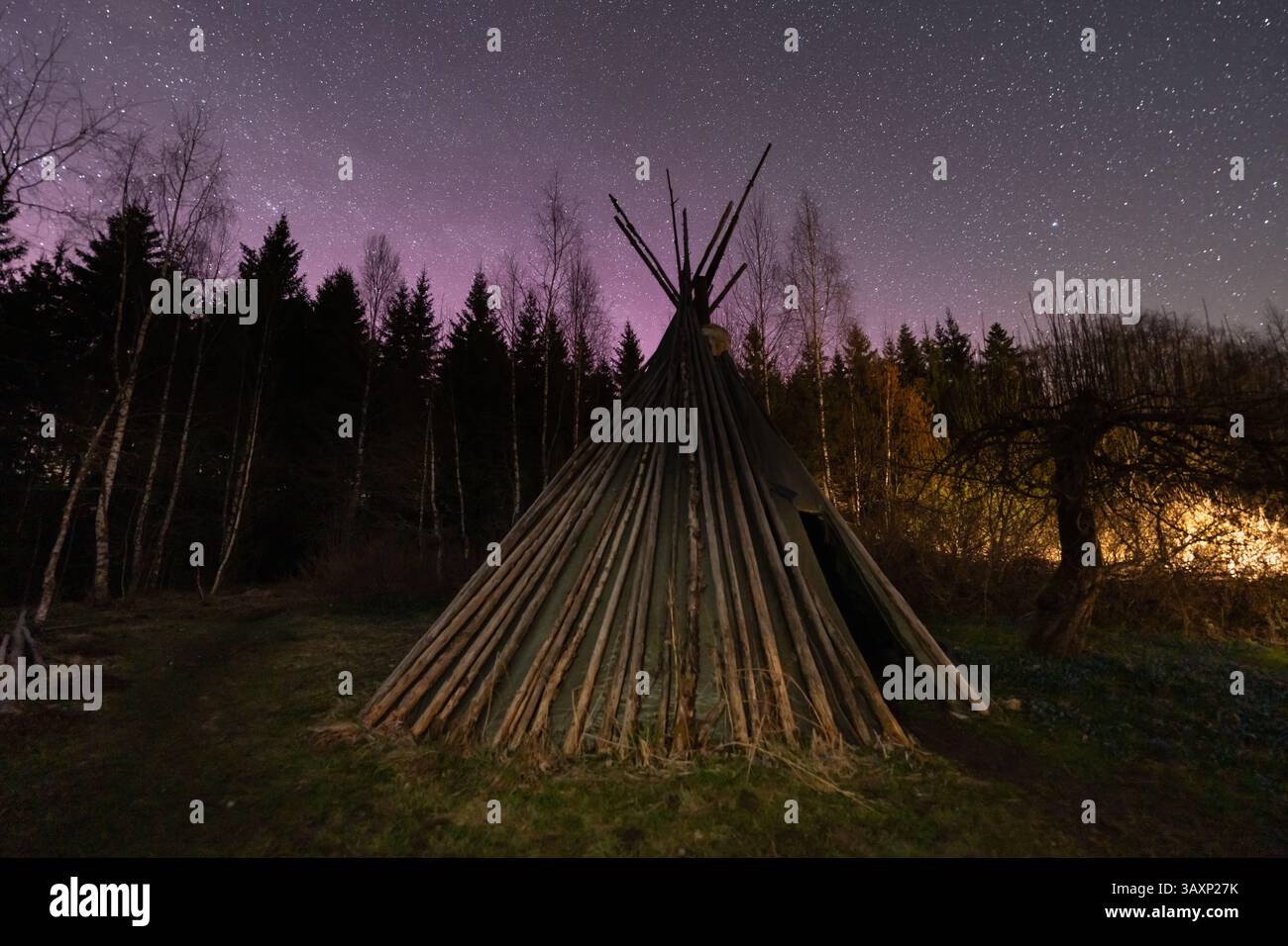 A traditional wooden tipi stands in a forest clearing under a magical ...