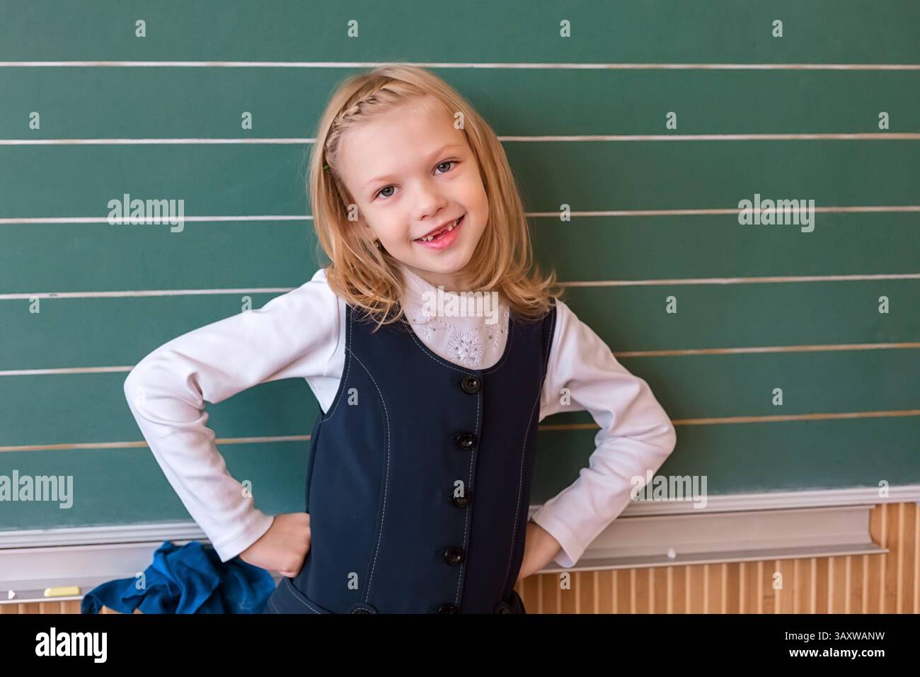 First grade pupil a girl writing on green blackboard at school lesson ...
