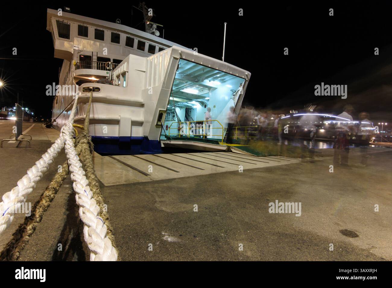 An illuminated ferry is docked at a harbor terminal at night with ...