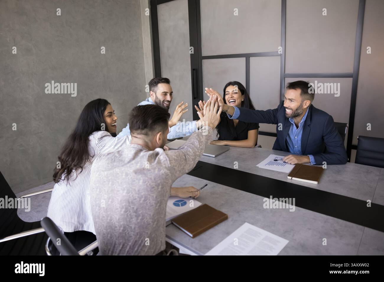 Team of professionals sits around conference table sharing high-five ...