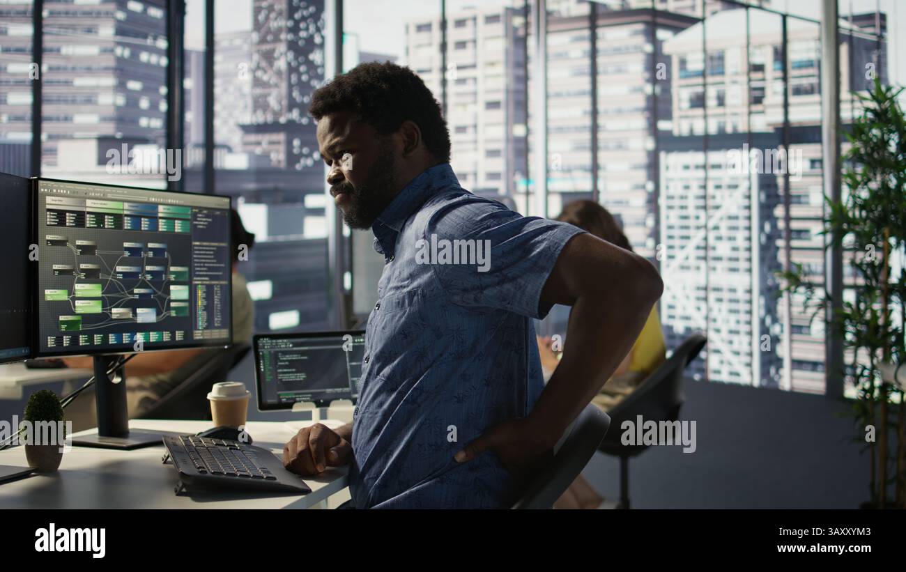 Employee with grimace on face stretches to relieve muscle strain while conducting code review to ...