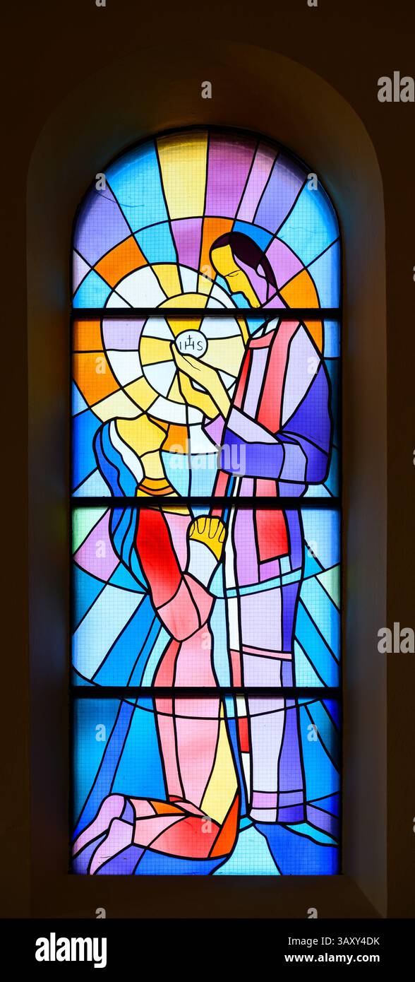 A priest giving the Eucharist to a kneeling young woman. A stained ...