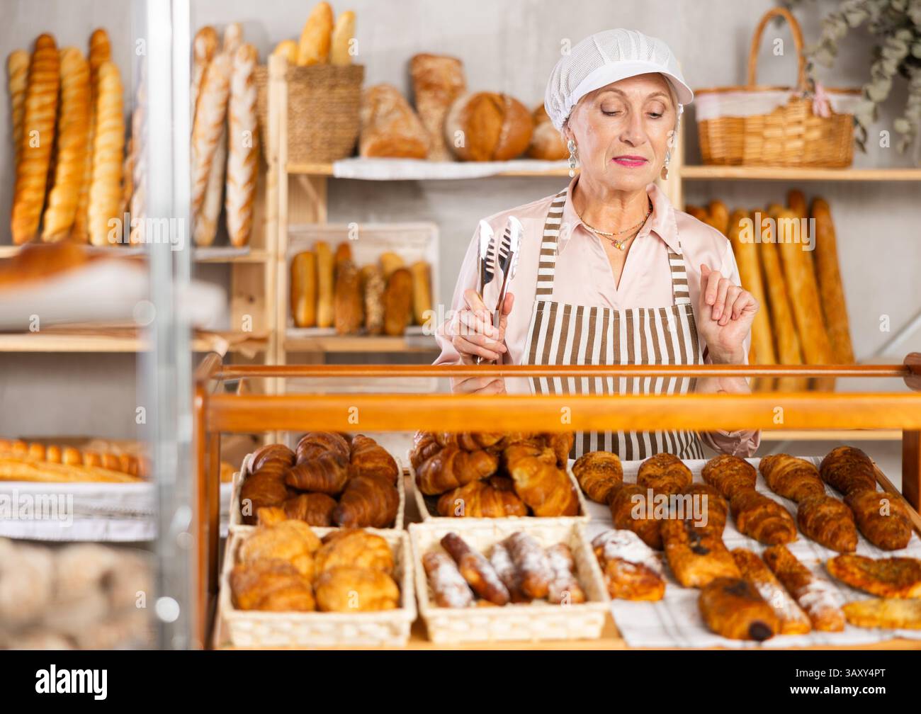 Senior woman employee puts croissants in window, arranges display of ...