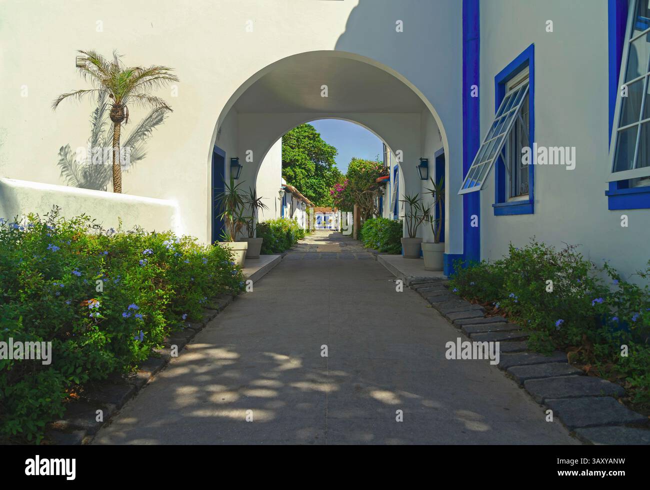A clean, white Mediterranean-style arch frames a narrow, sunlit walkway ...