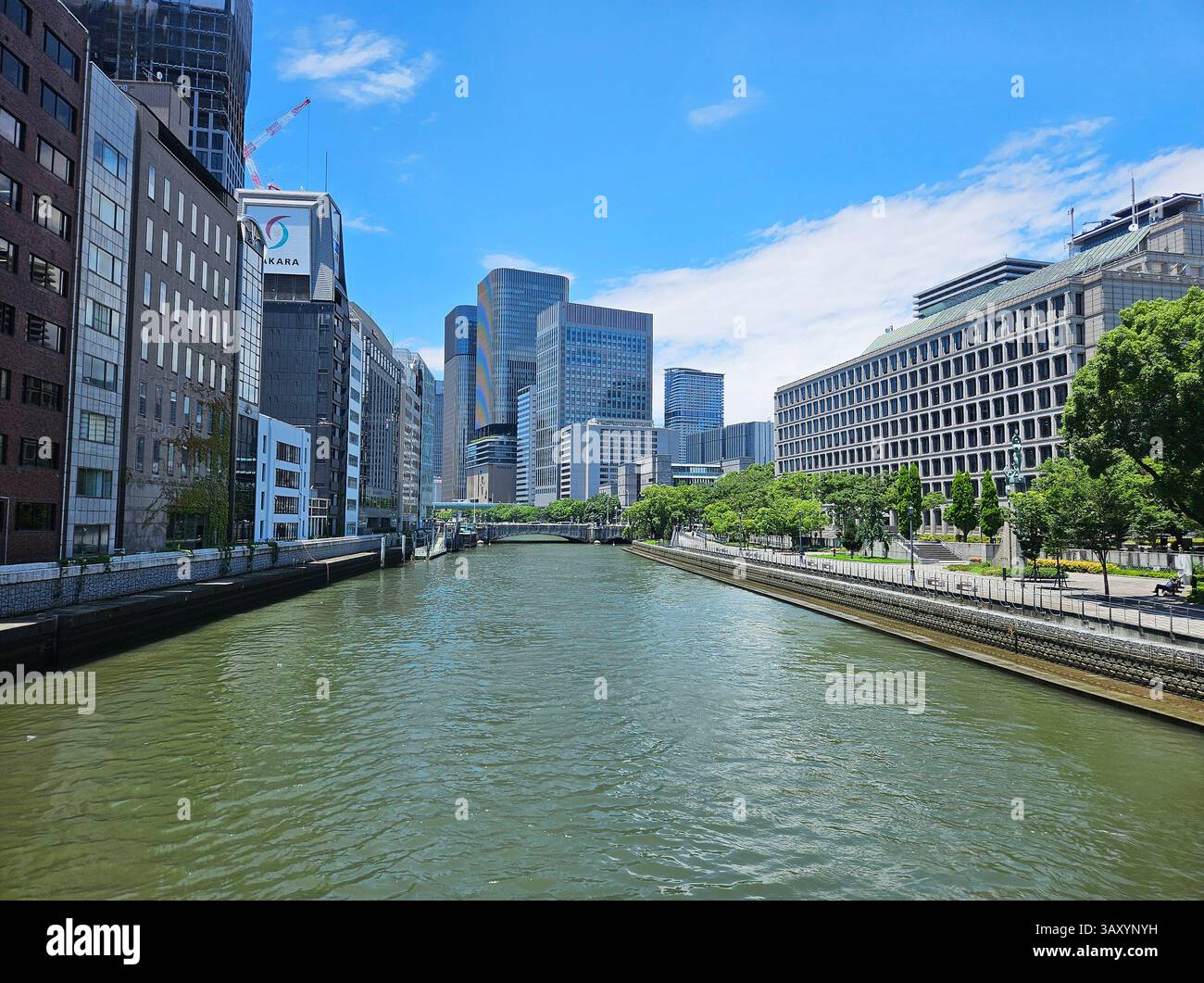 Modern cityscape reflecting under a bright blue sky alongside a serene river in the heart of ...