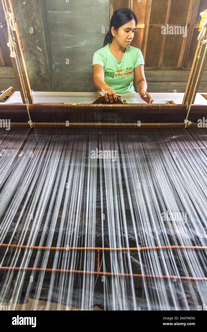 A young Filipina artisan weaves piña fibers on a traditional loom in ...
