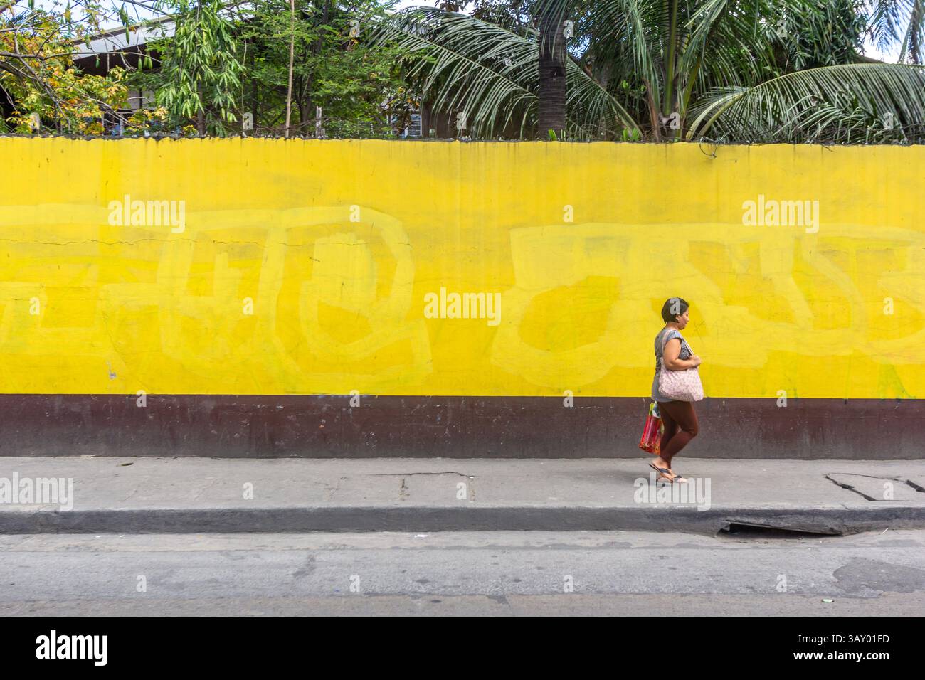 A woman walks past a wide yellow wall in Manila, Philippines, adding a ...