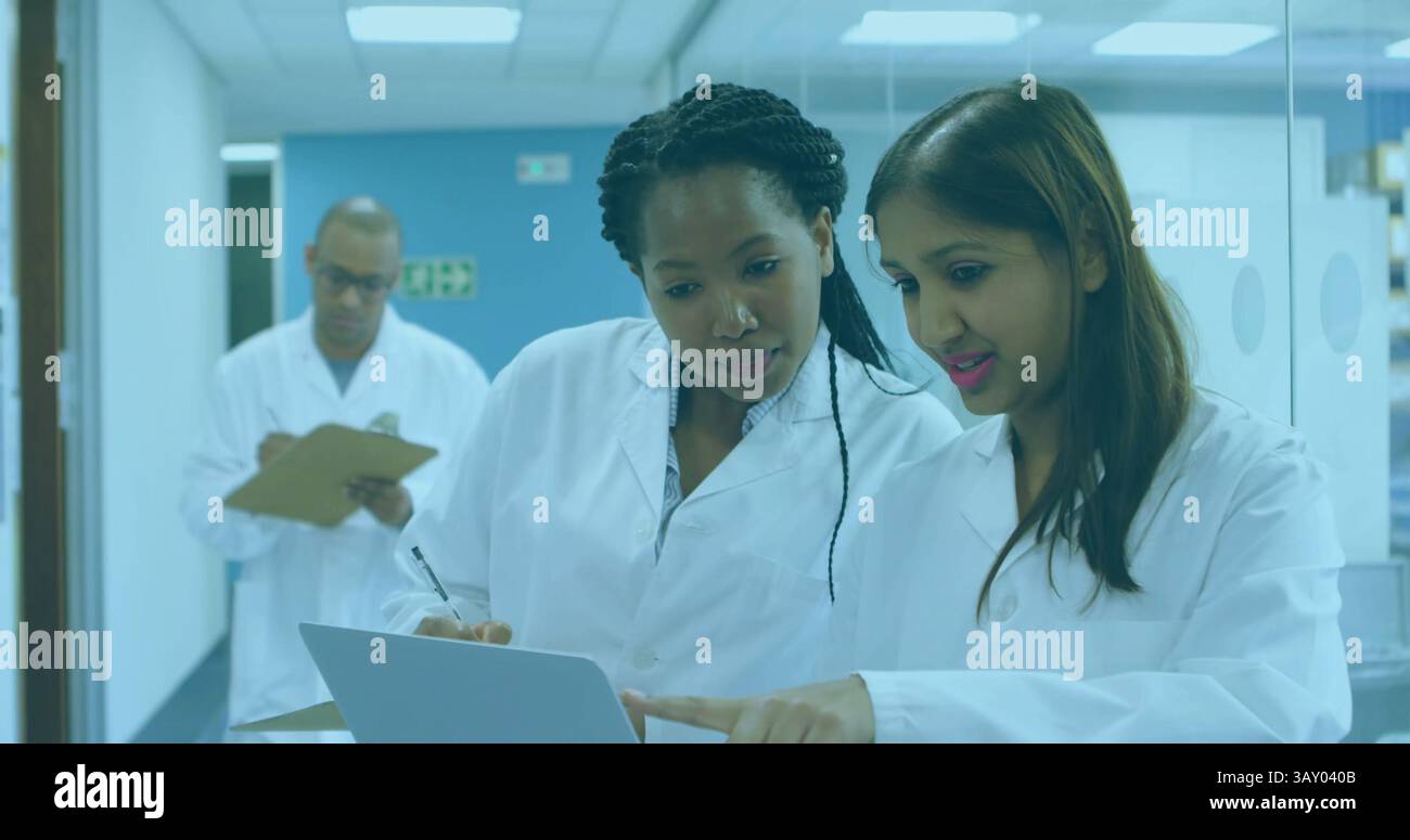 two female scientists wearing lab coats are examining laptop in ...