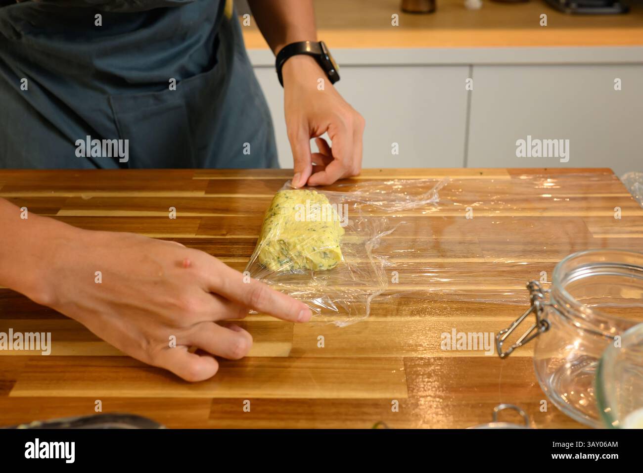 Man wrapping freshly made compound butter in plastic wrap on wooden ...