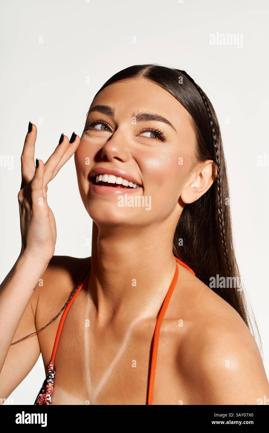 A young woman with a sun tan applies sunscreen while smiling joyfully ...