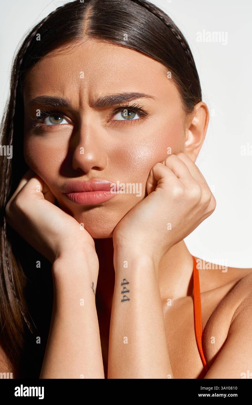 A pretty young woman with a sun tan looks thoughtful, shielding her ...