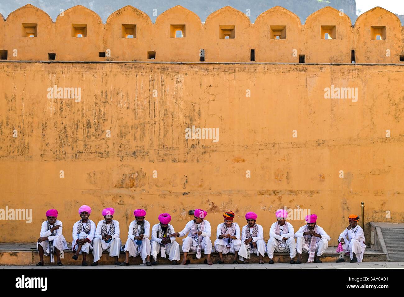 Men wearing traditional attire sit in the shade prior to conducting a ...