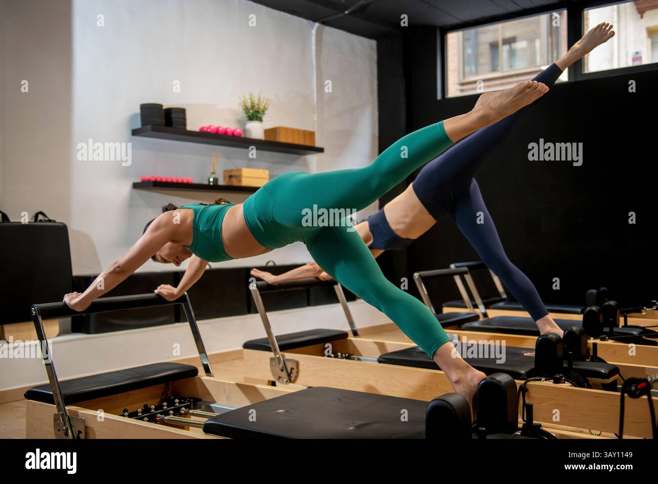 Two women practicing pilates exercises on reformer beds, showcasing ...