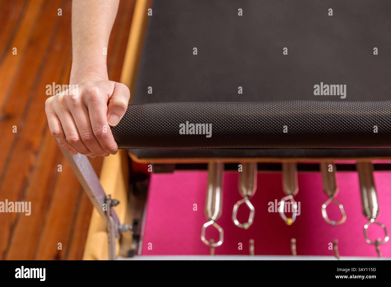 A person is gripping the handle of a reformer, engaging in a Pilates ...
