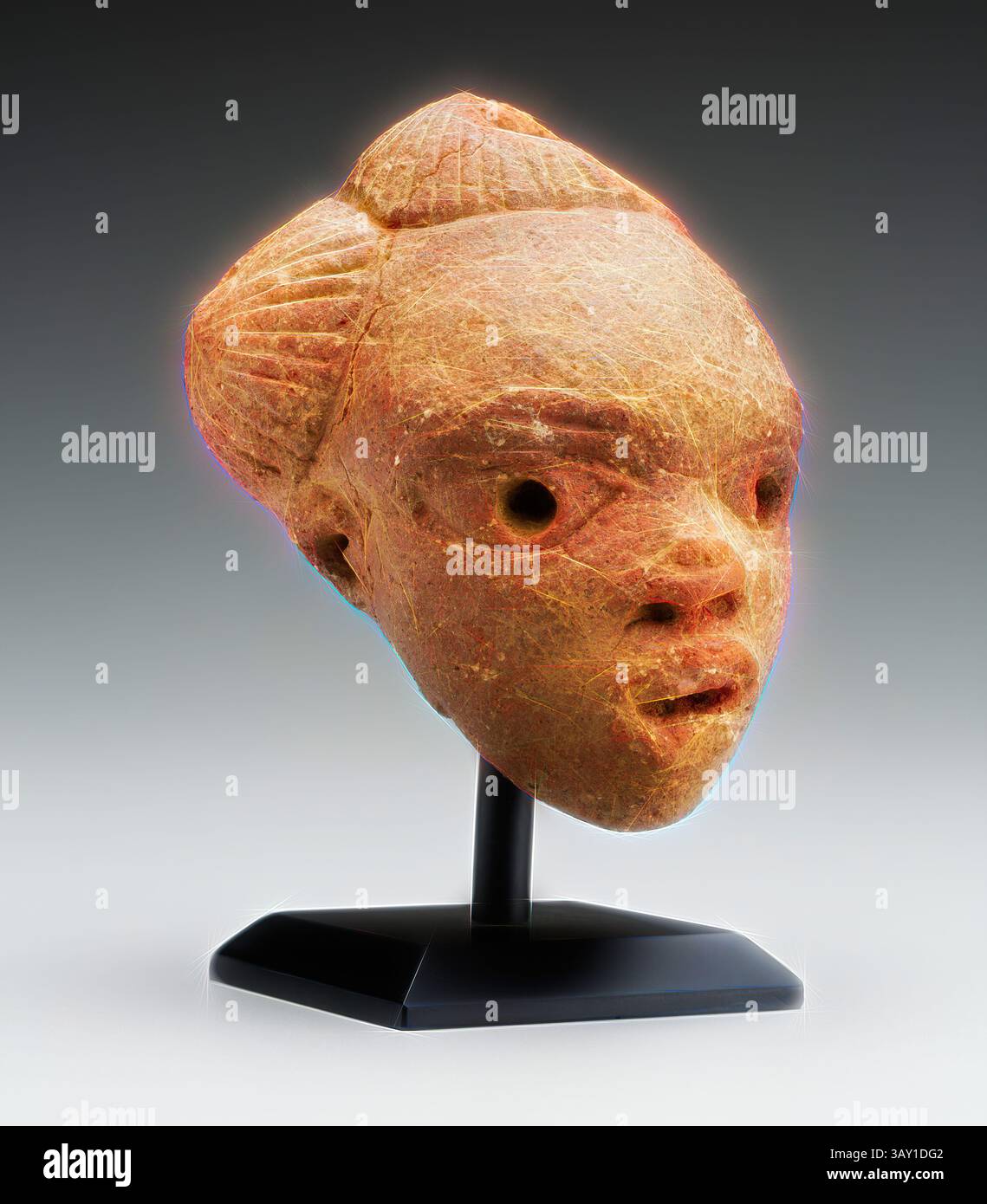 A carved stone sculpture depicting a stylized human face, characterized ...