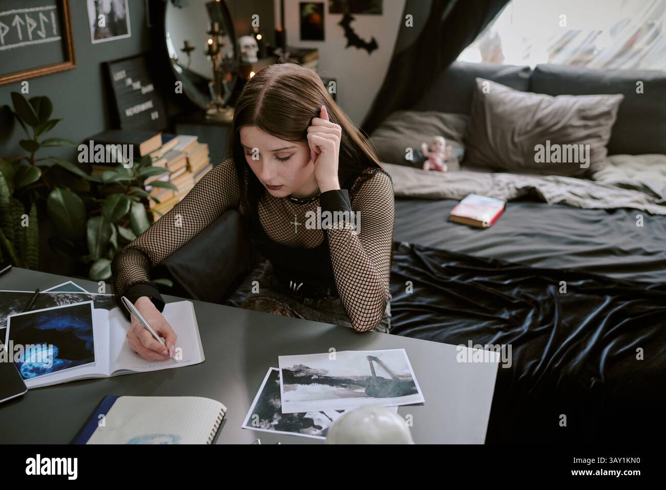 High angle shot of goth girl sitting at table and drawing in notepad ...