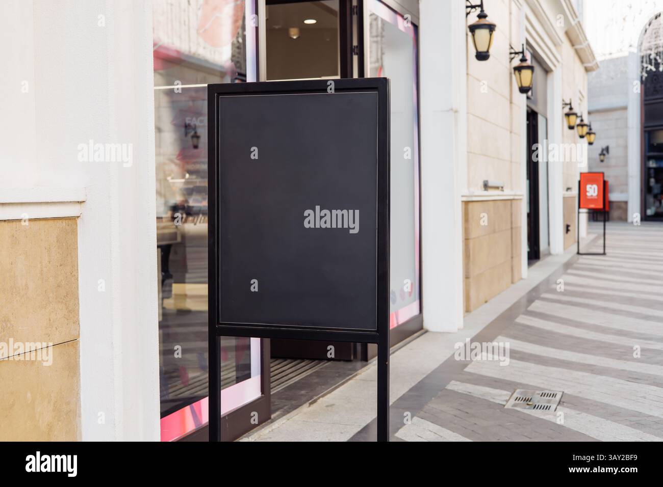Mockup blank sign stands on a busy sidewalk in a shopping area. The ...