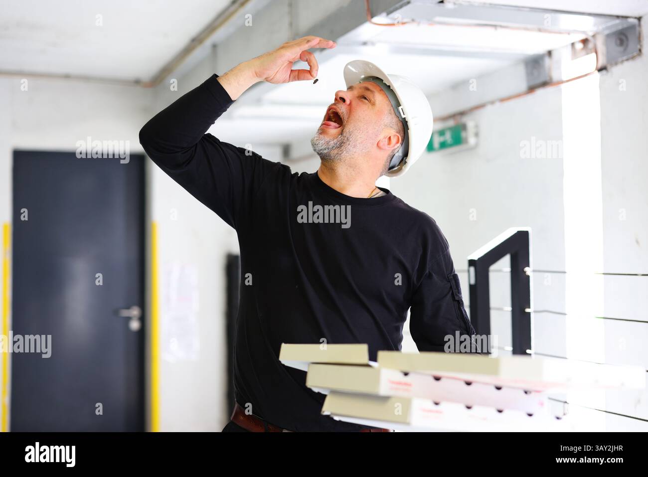Construction worker with pizza boxes pretending to eat a small item ...