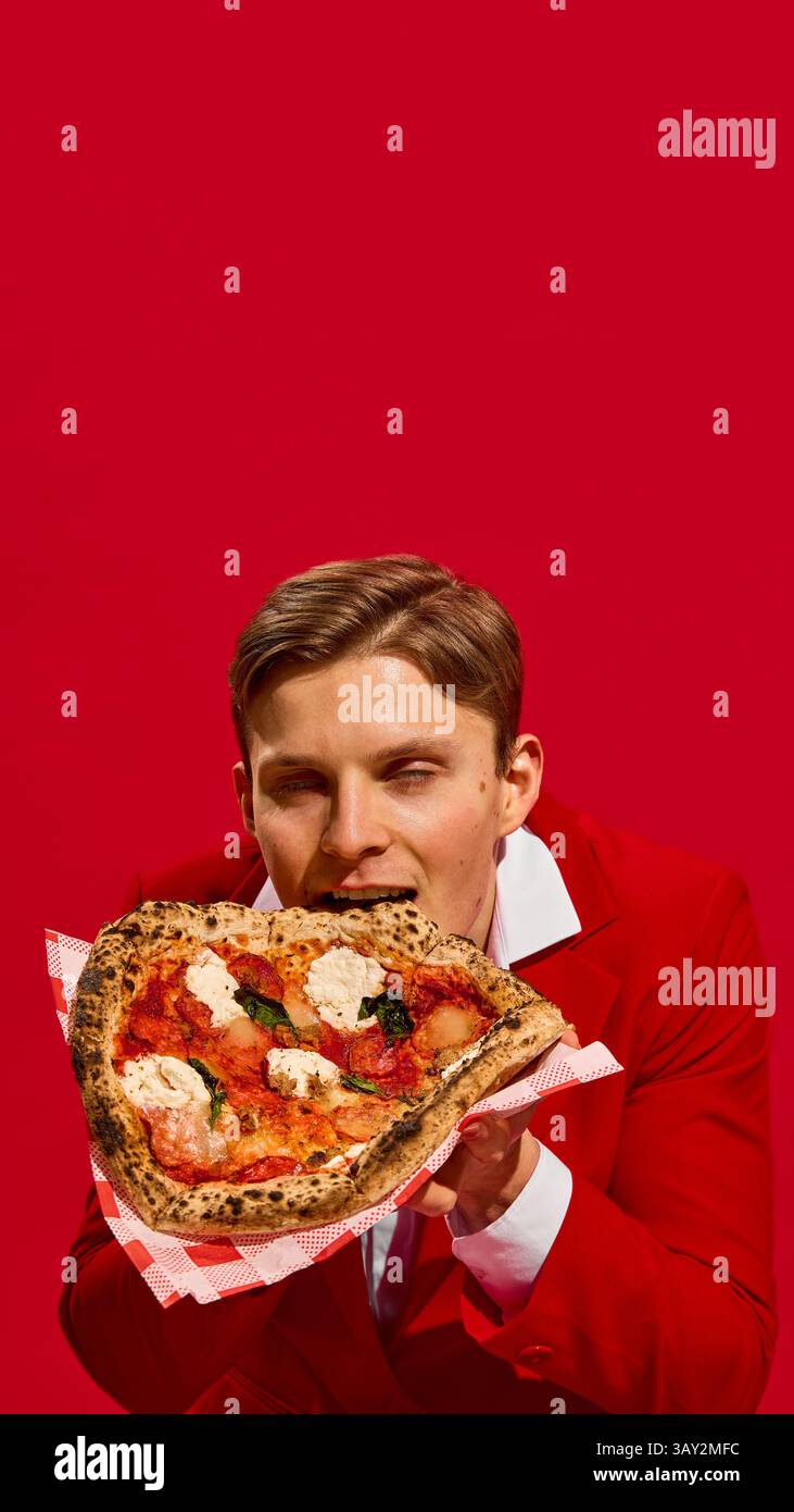 Satisfied young man in red suit biting delicious Italian pizza with ...