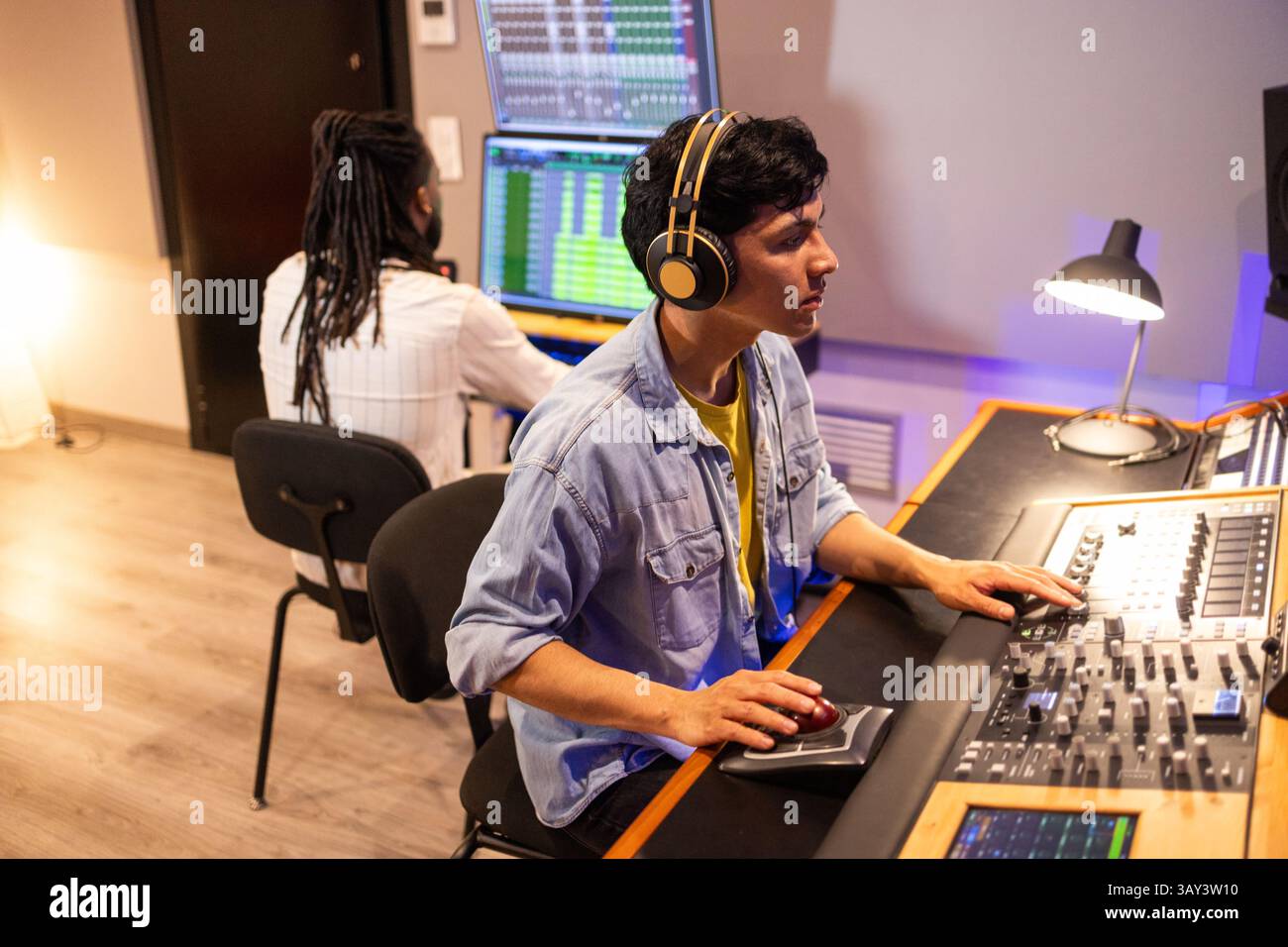 Two audio engineers work in a recording studio, wearing headphones and ...