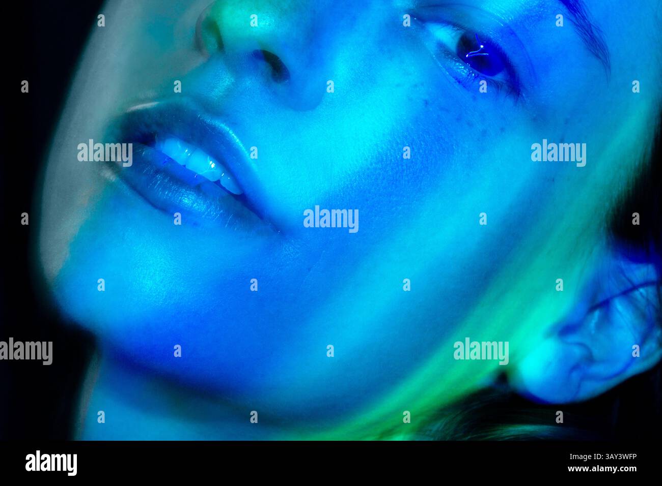 A close up shot of a woman is face bathed in vibrant blue neon light ...