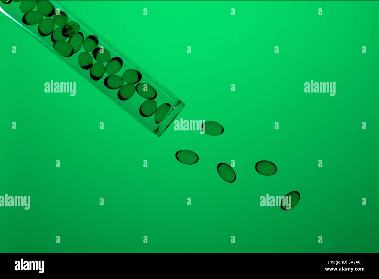 Omega-3 and Vitamin D capsules spill from a clear tilted test tube onto ...