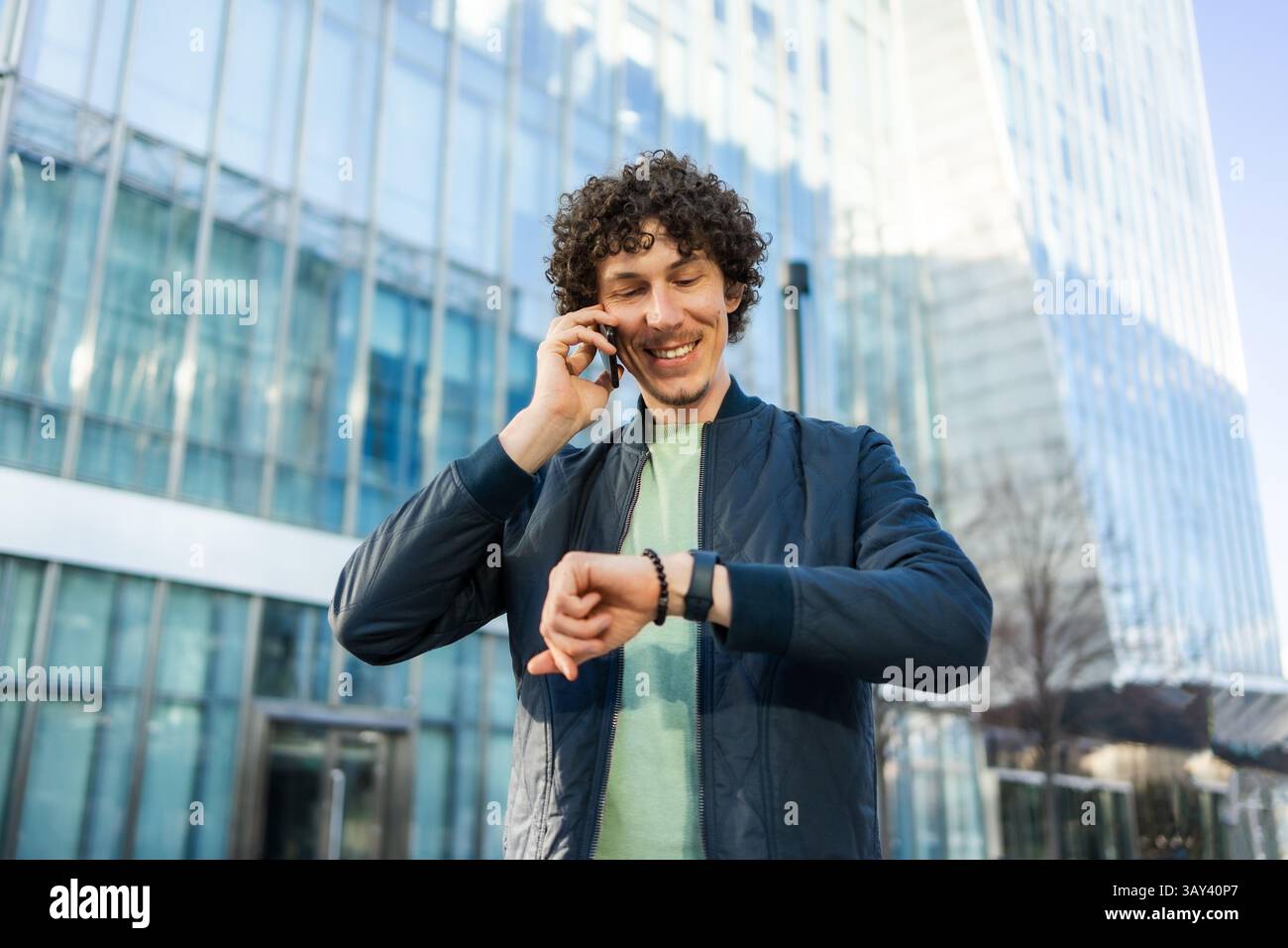 Smiling man in casual attire checks the time on his smartwatch while ...