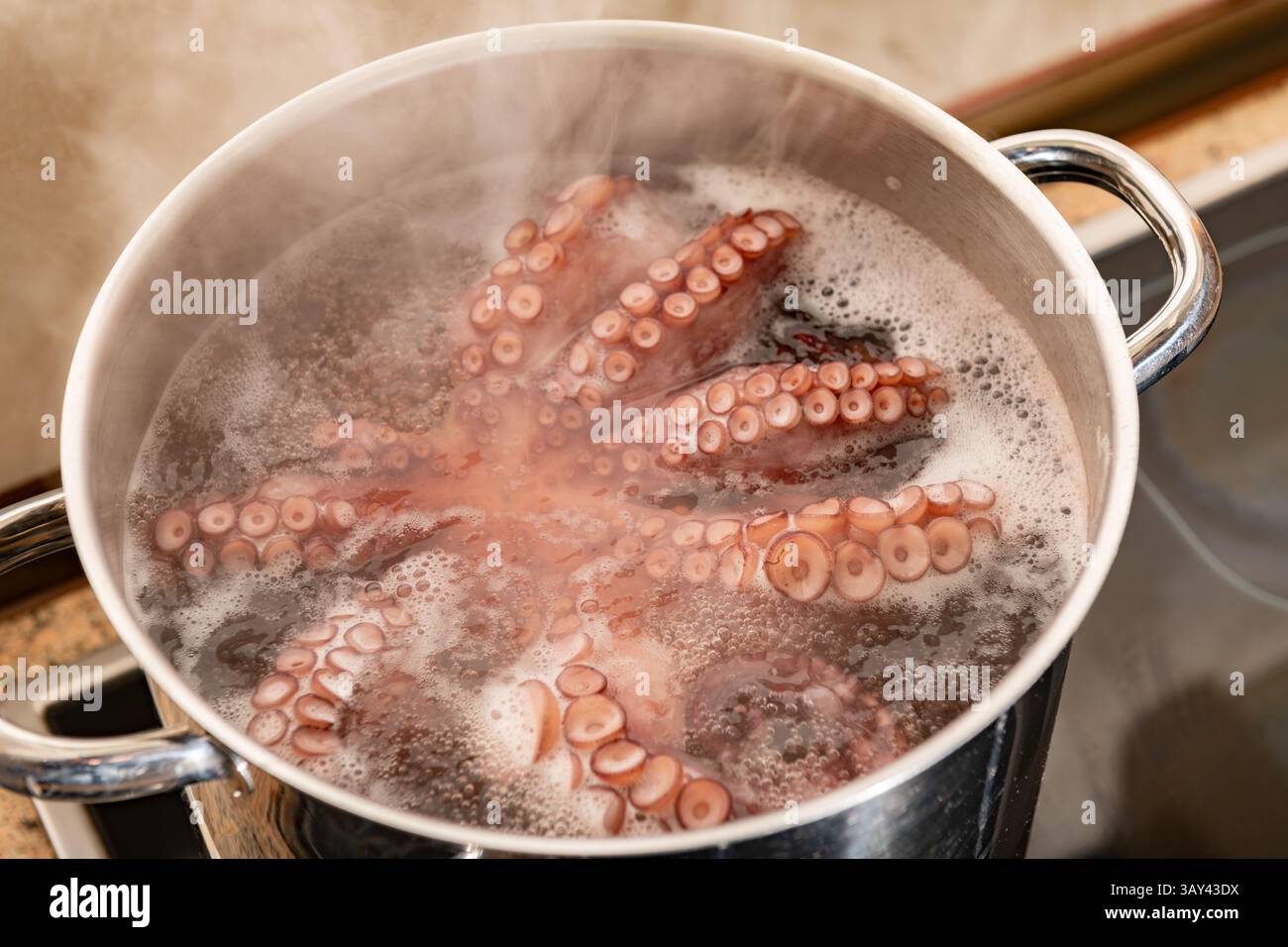 Octopus tentacles are boiling in a stainless steel pot, steam rising ...