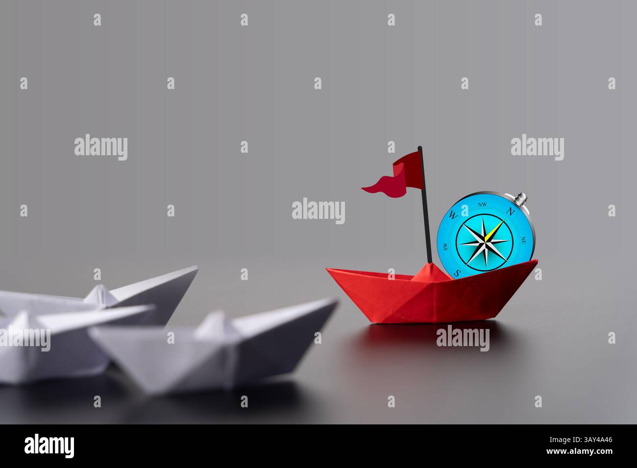 Red paper boat perched on a compass rose, surrounded by white boats ...
