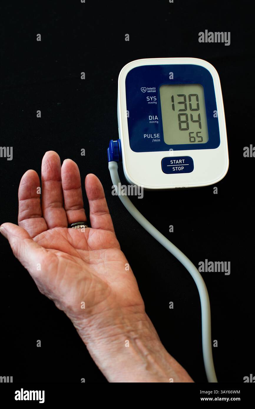 A hand extends towards a digital blood pressure monitor reading 130 ...