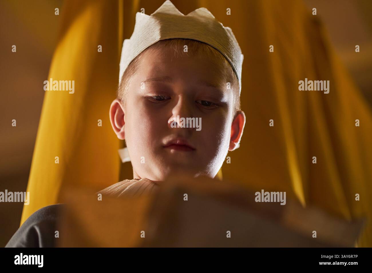 Backlit portrait of concentrated little boy wearing costume of king revising lines before going ...
