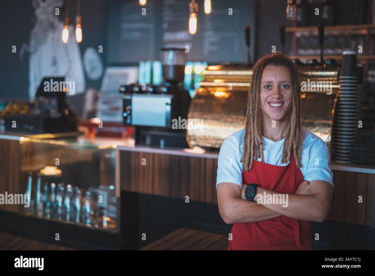 Young adult male barista standing smiling behind counter in cafe with ...