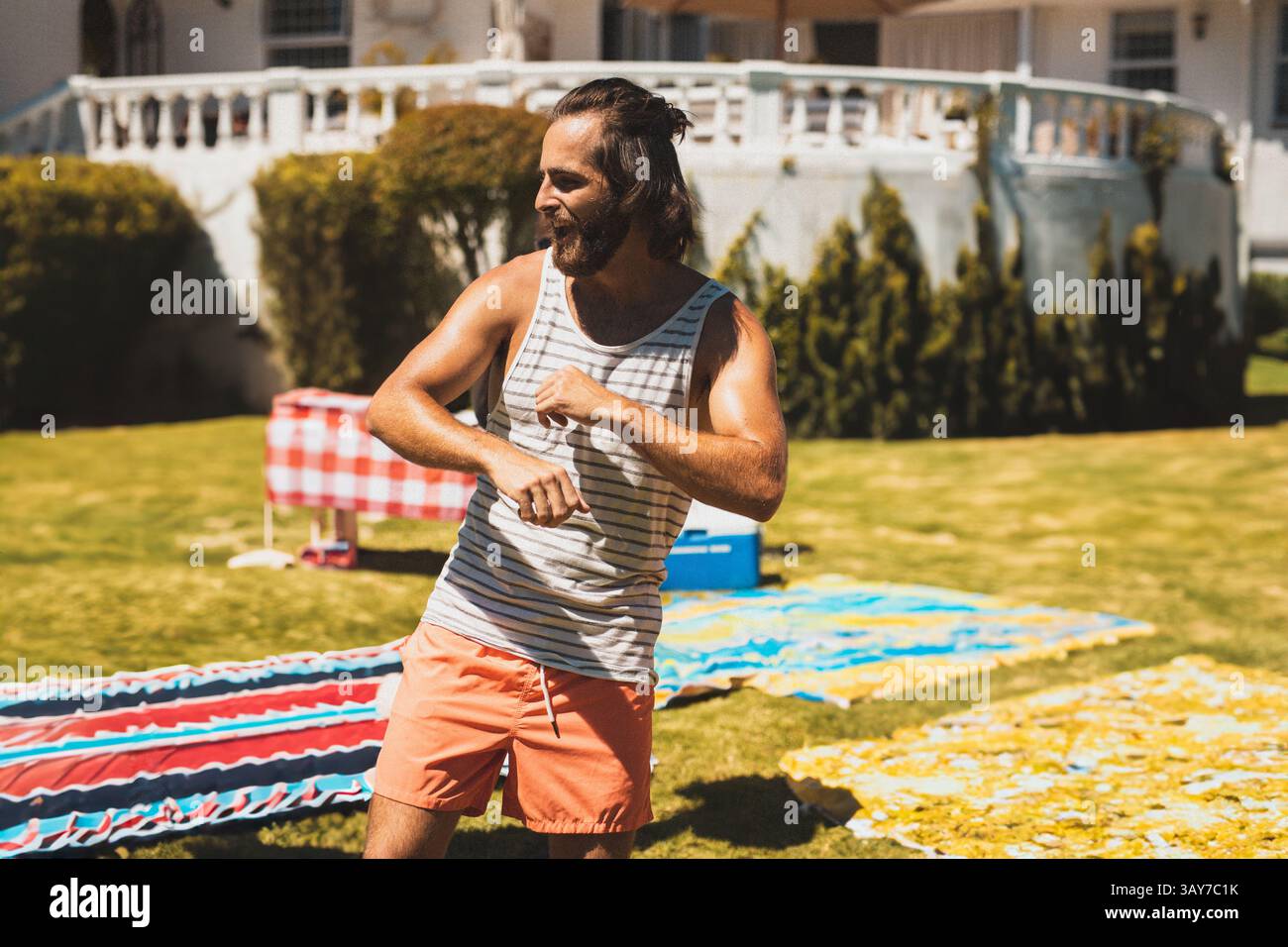 Man dancing on lawn by white two-story house, with beach towels, picnic ...
